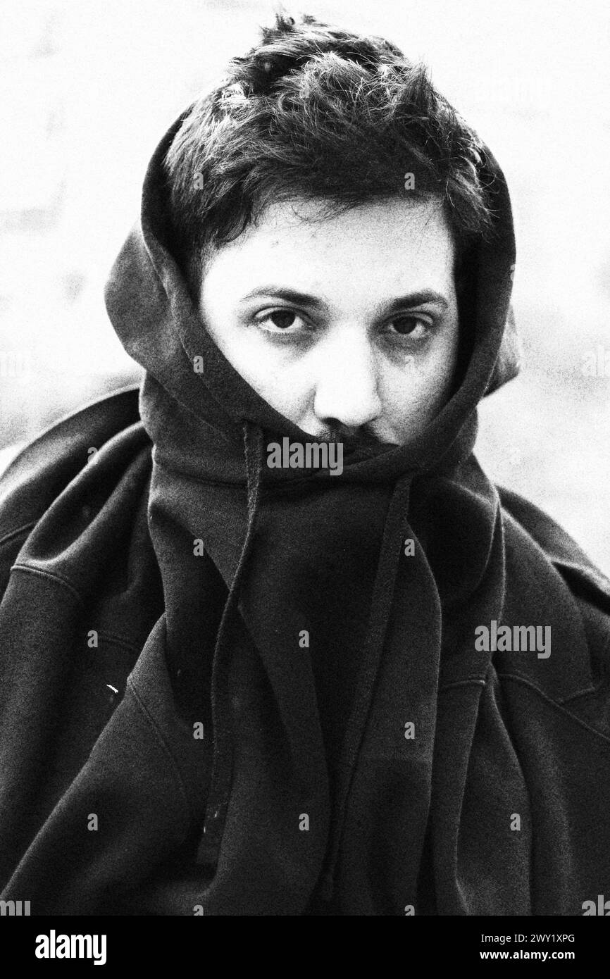 Concealed behind his hands, a young man shields his face, veiling his ...