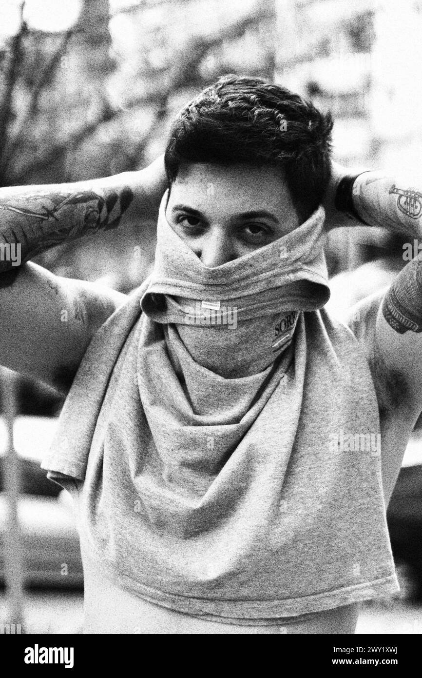 Concealed behind his hands, a young man shields his face, veiling his ...