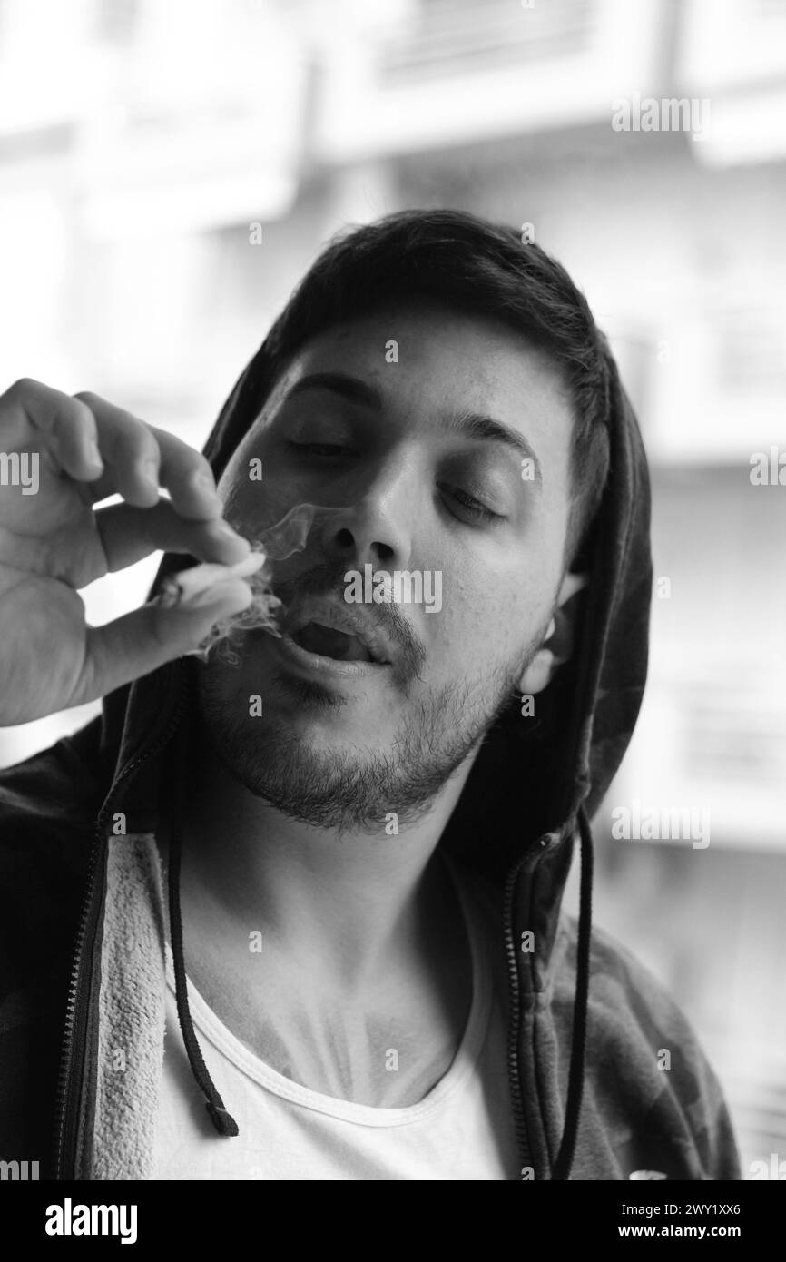 In the dim light, a young man inhales from a joint, enveloped in the ...