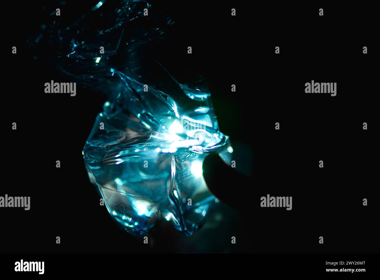 A transparent plastic bottle compressed and containing water, held by a ...