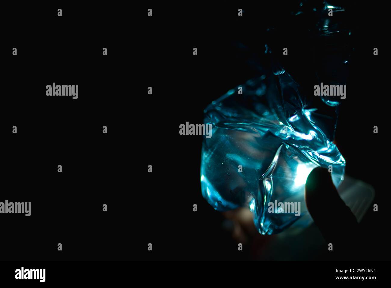 A transparent plastic bottle compressed and containing water, held by a ...