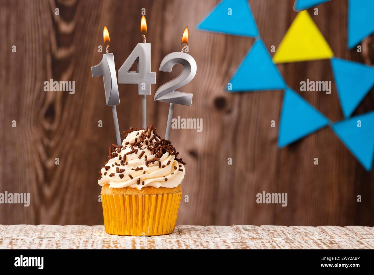 Burning candle - birthday number 142 on wooden background with pennants ...