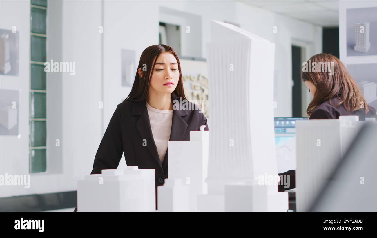 Architect Analyzing Blueprints And 3d Building Models At Design Table Trying To Develop New