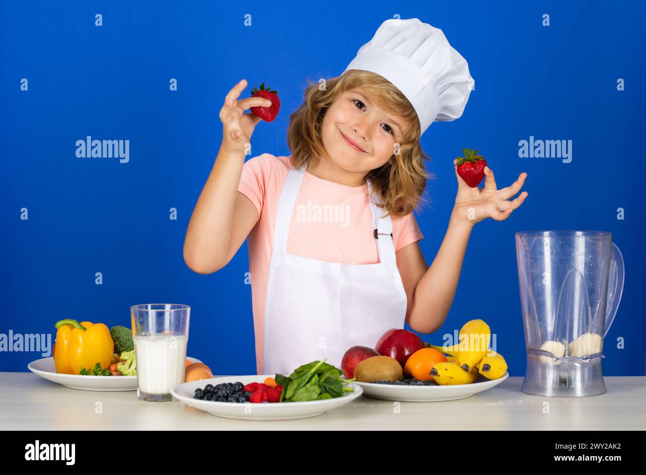 Child chef hold strawberries isolated on blue. Funny little kid chef ...
