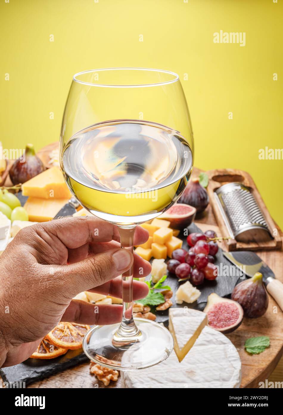 Glass of white wine in a man's hand with variety of sliced cheeses with ...