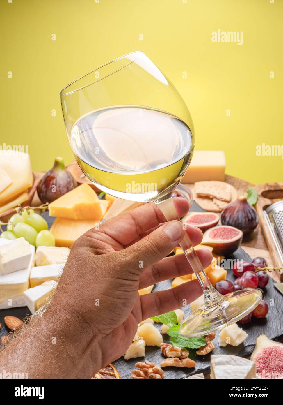 Glass of white wine in a man's hand with variety of sliced cheeses with ...