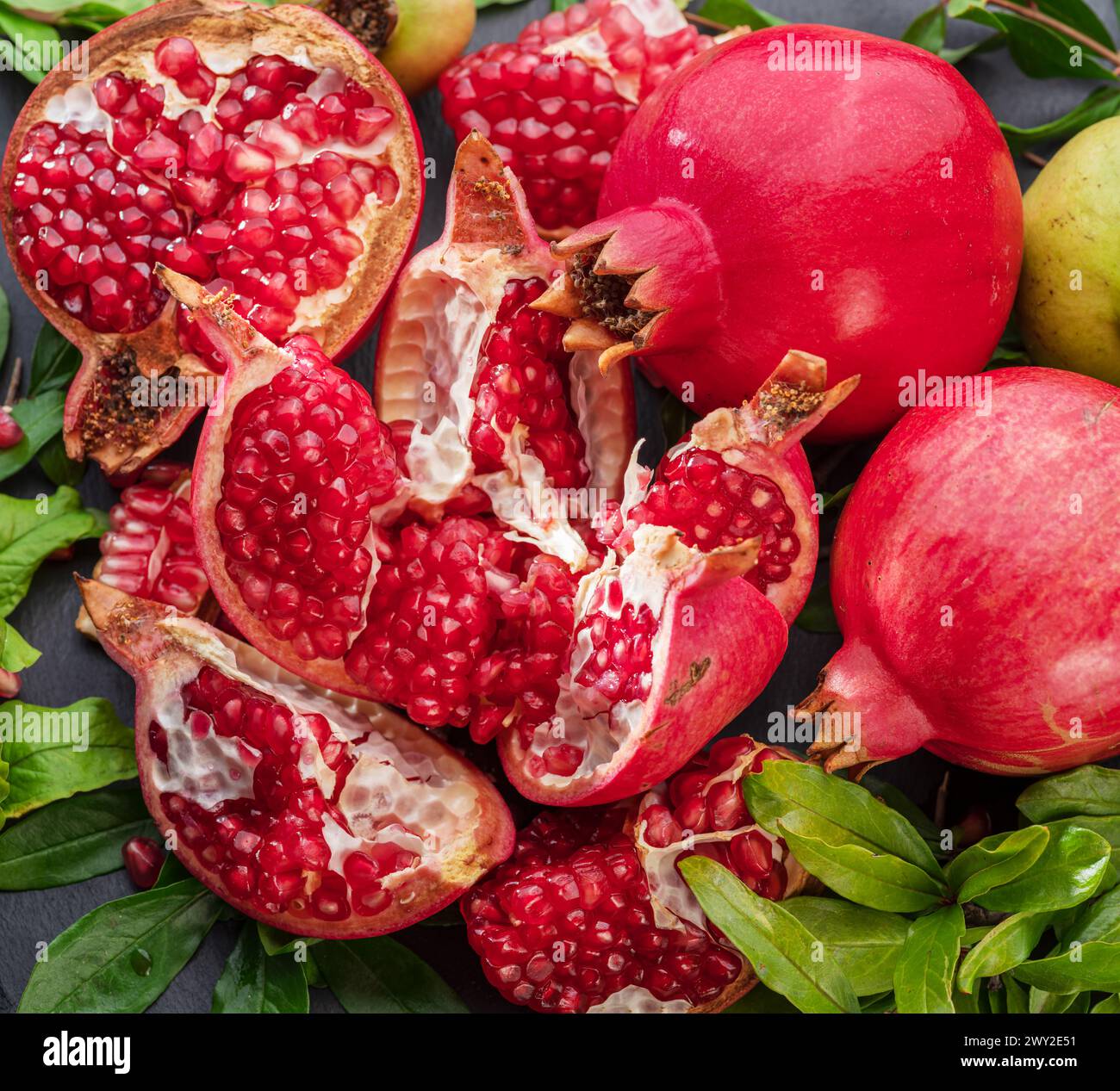 Ripe pomegranate fruits with slices and pomegranate tree leaves on a ...