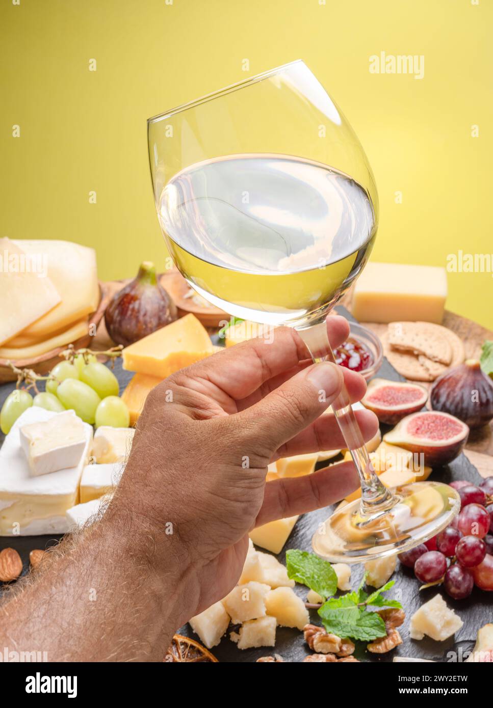 Glass of white wine in a man's hand with variety of sliced cheeses with ...