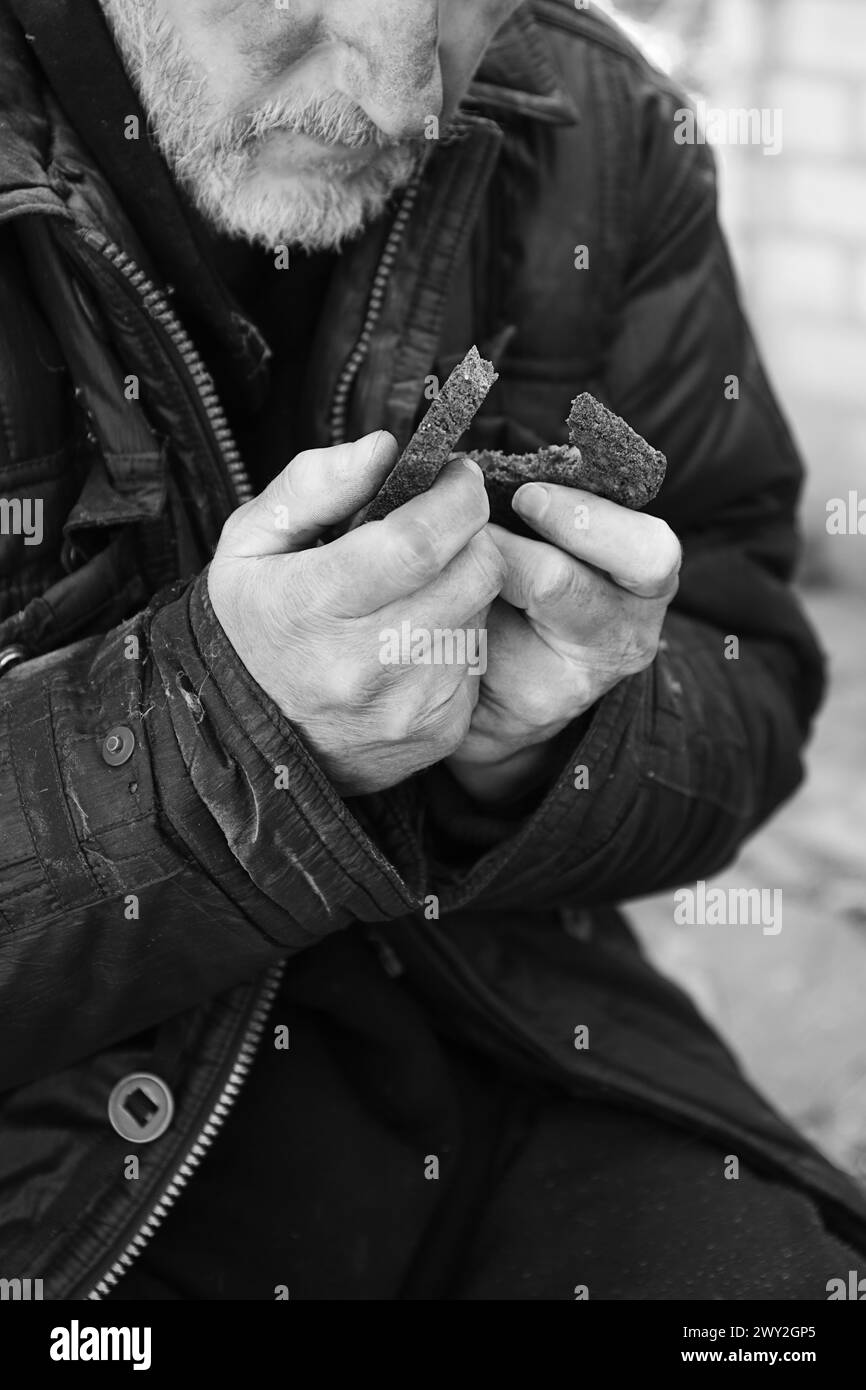 Poor homeless man holding piece of bread outdoors, closeup. Black and ...