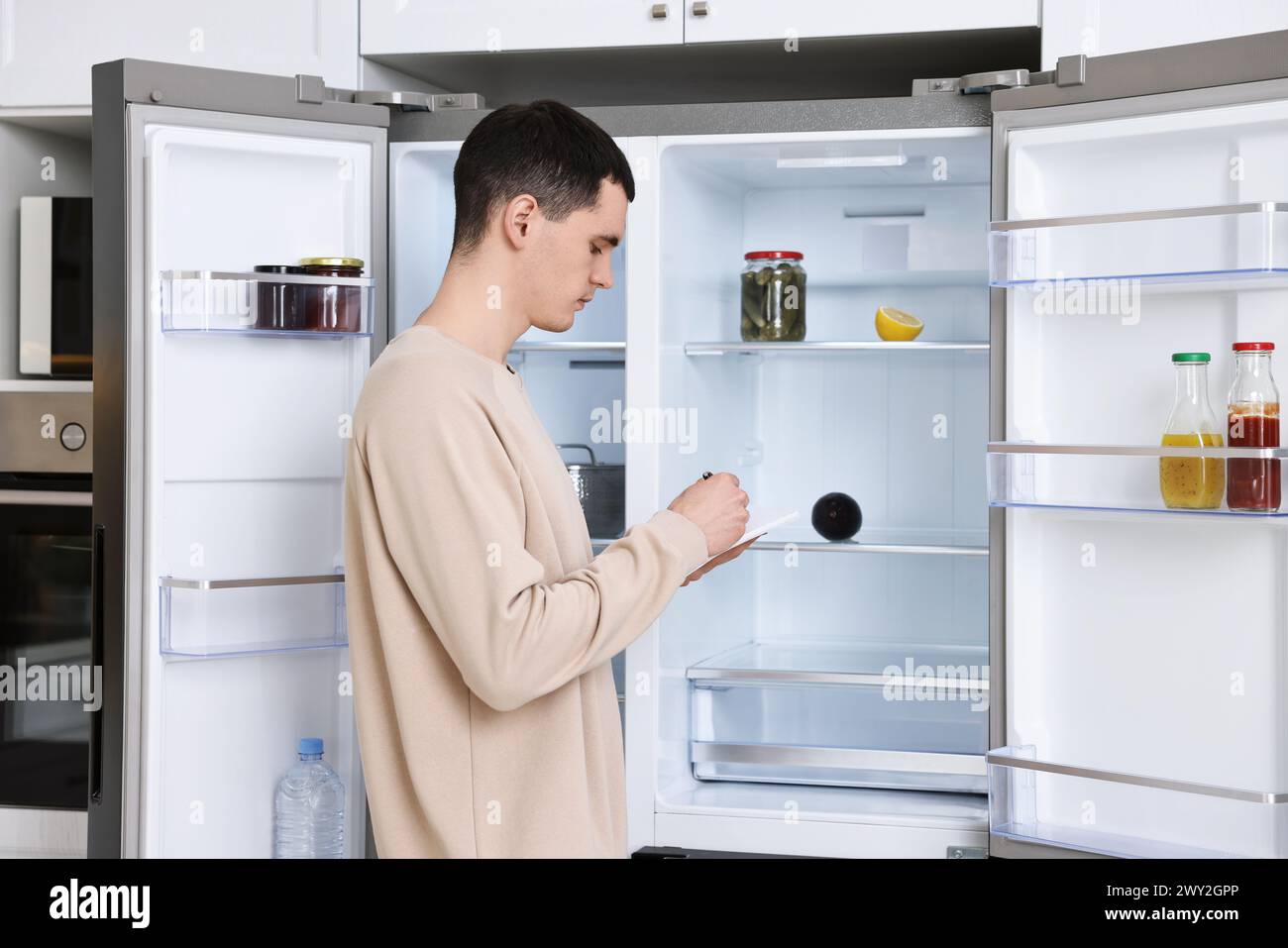 Man writing notes near empty refrigerator in kitchen Stock Photo - Alamy