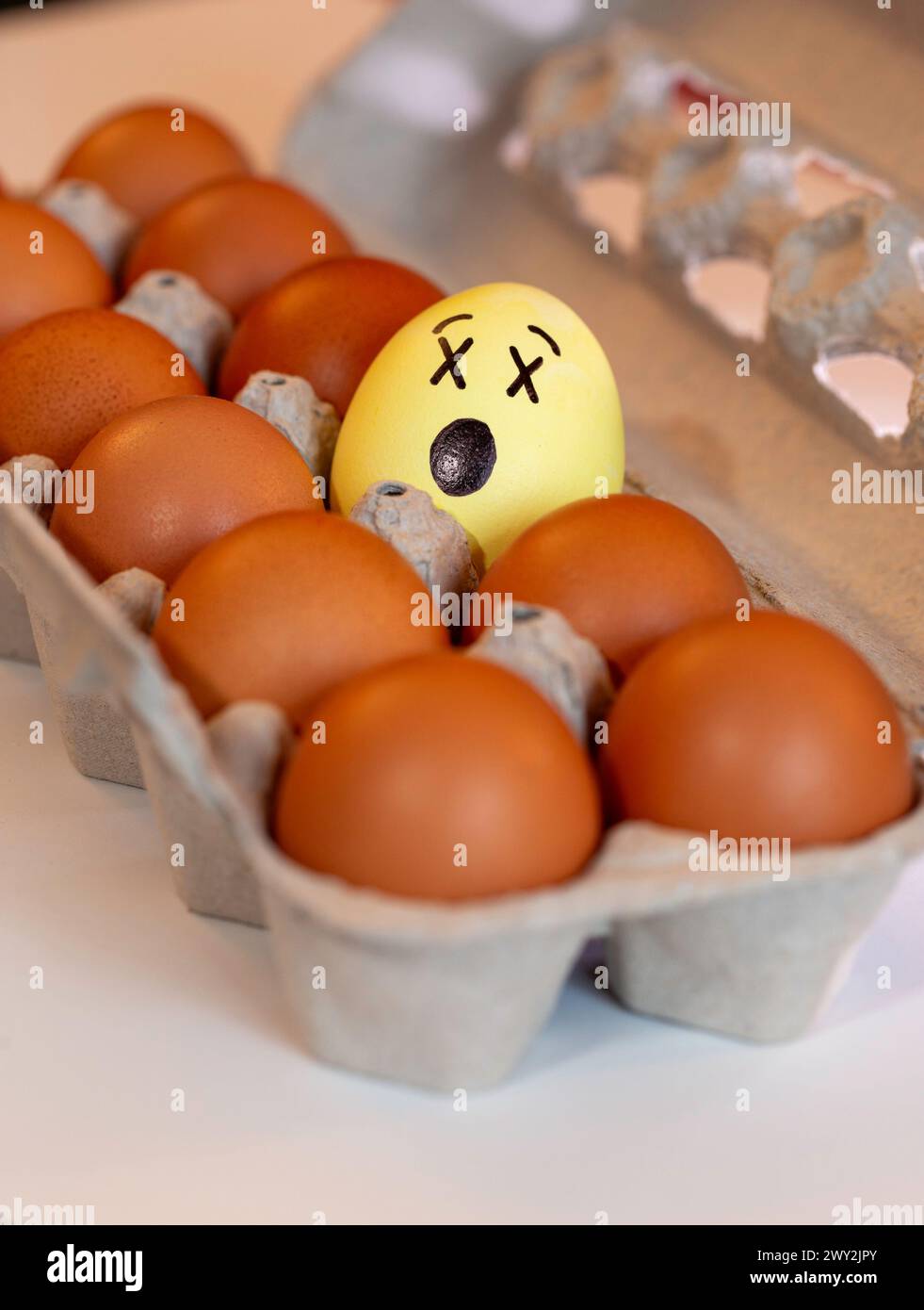Still life of dozen brown eggs in a carton with one Knocked out Emoji ...