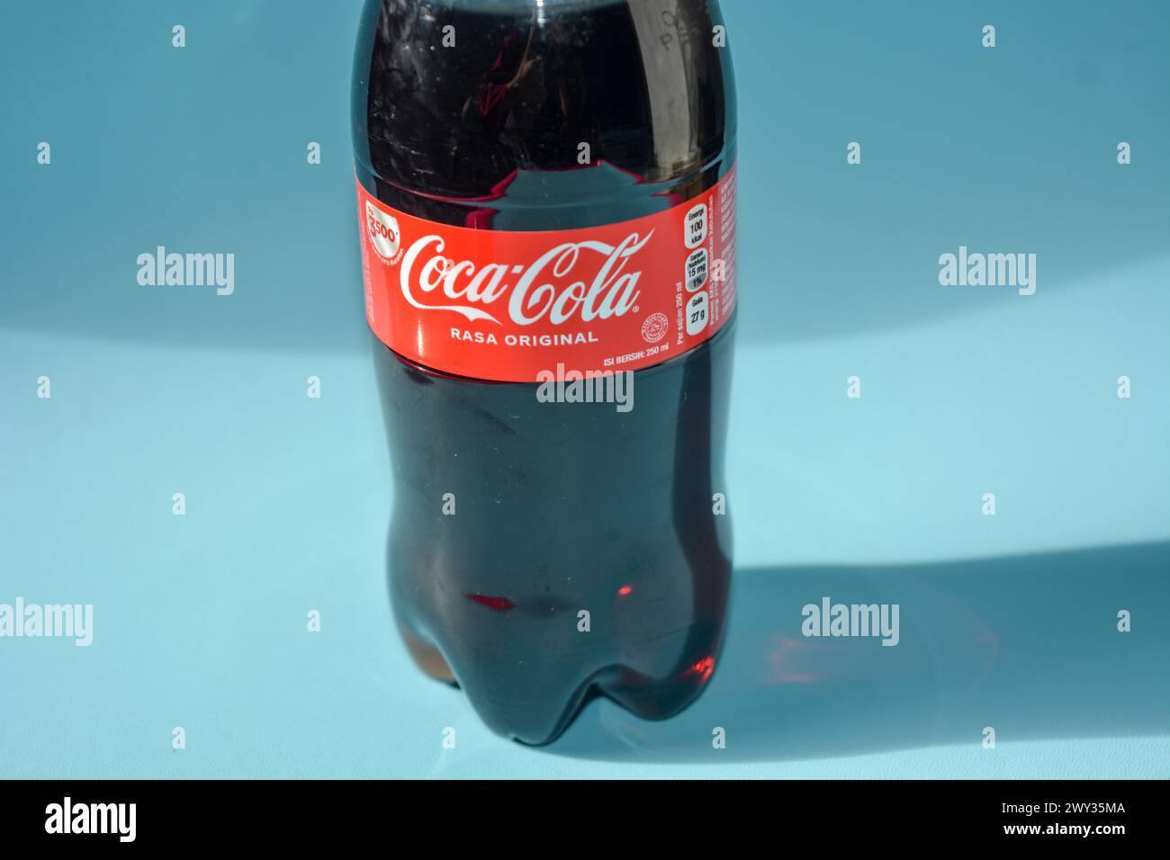 Close up view of a hand holding a Coca Cola product. Against a blue ...