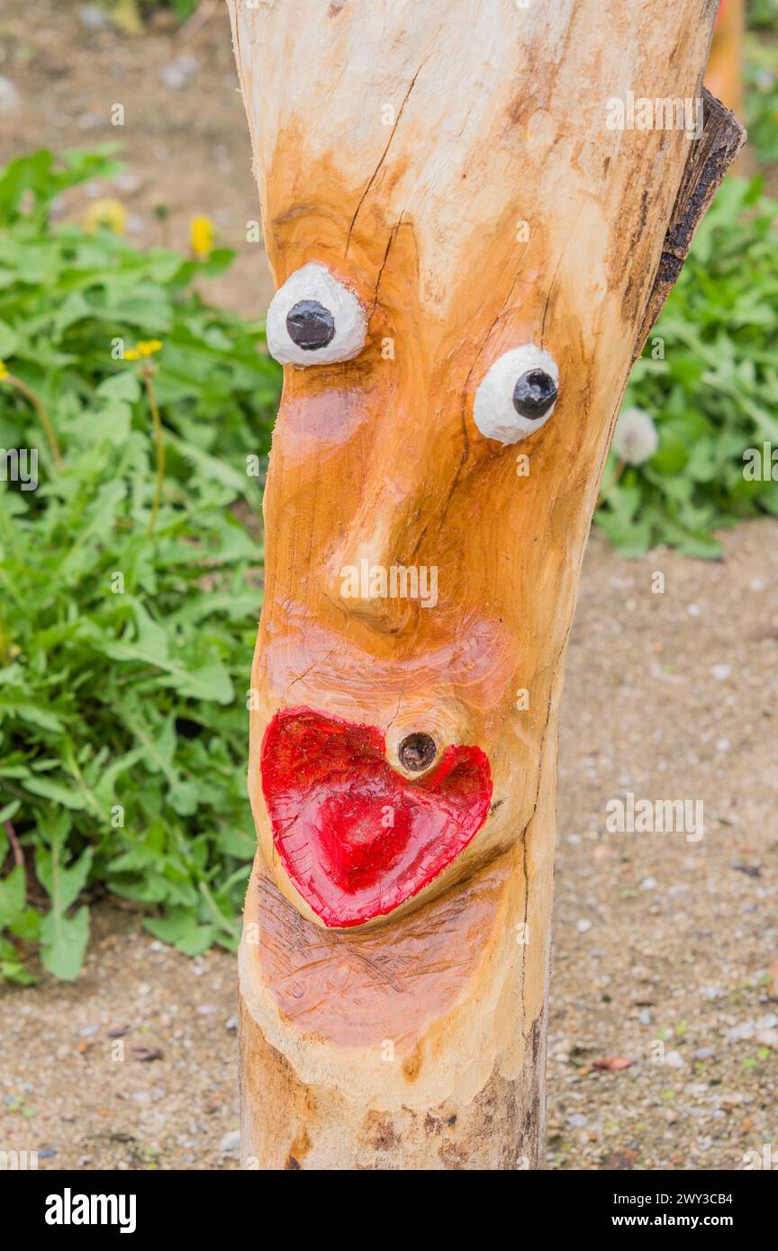 Hand-carved wooden face with a surprised look and red lips in nature ...