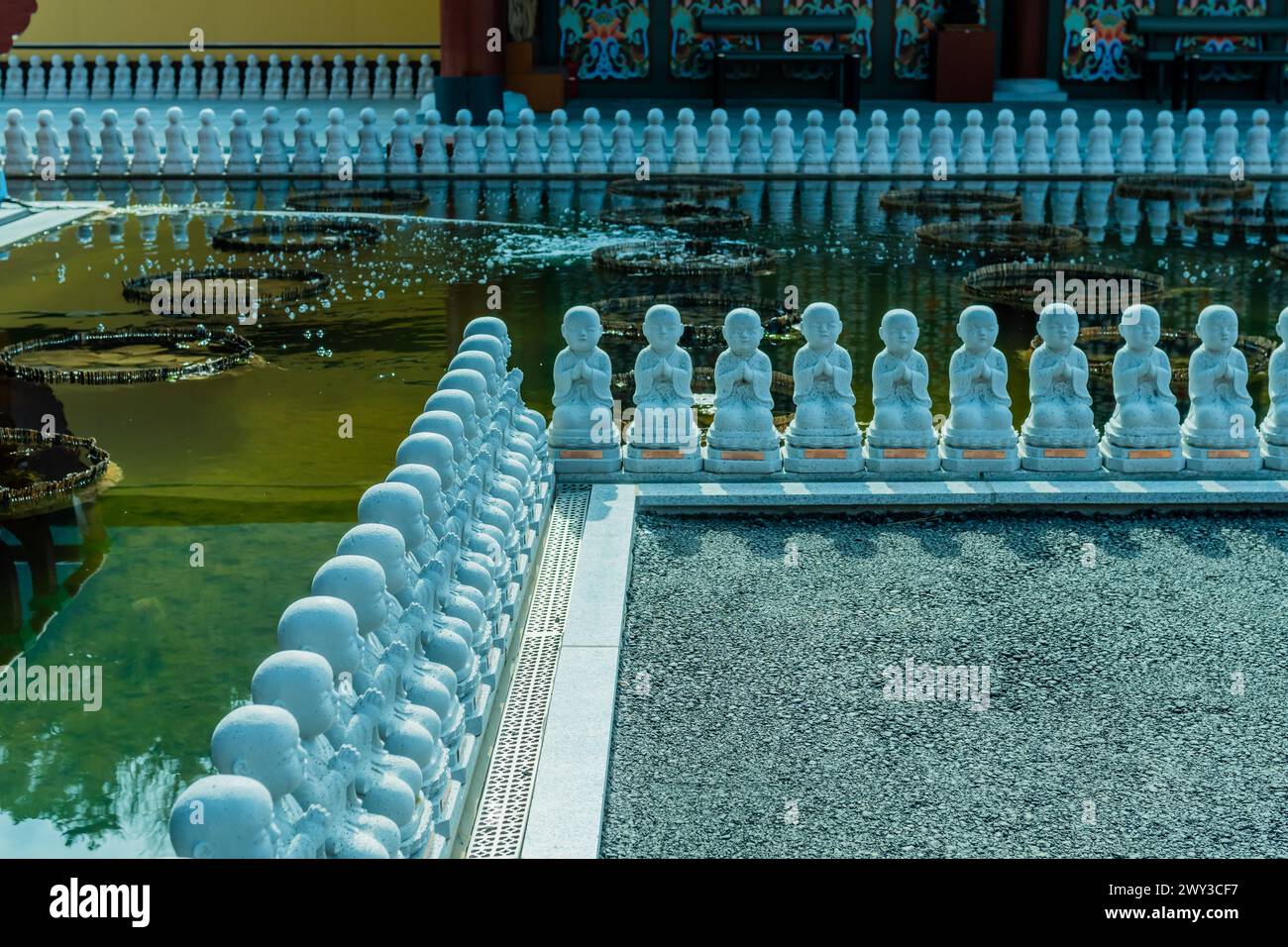 Small statues of praying Buddha line man made pond at Manbulsa Temple ...