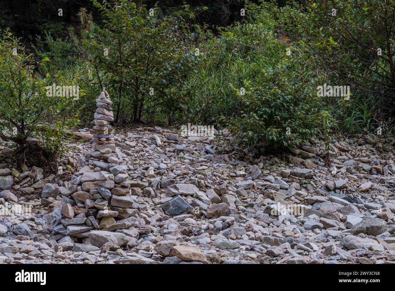 Pebble stack in dry rocky riverbed with trees and bushes in background ...