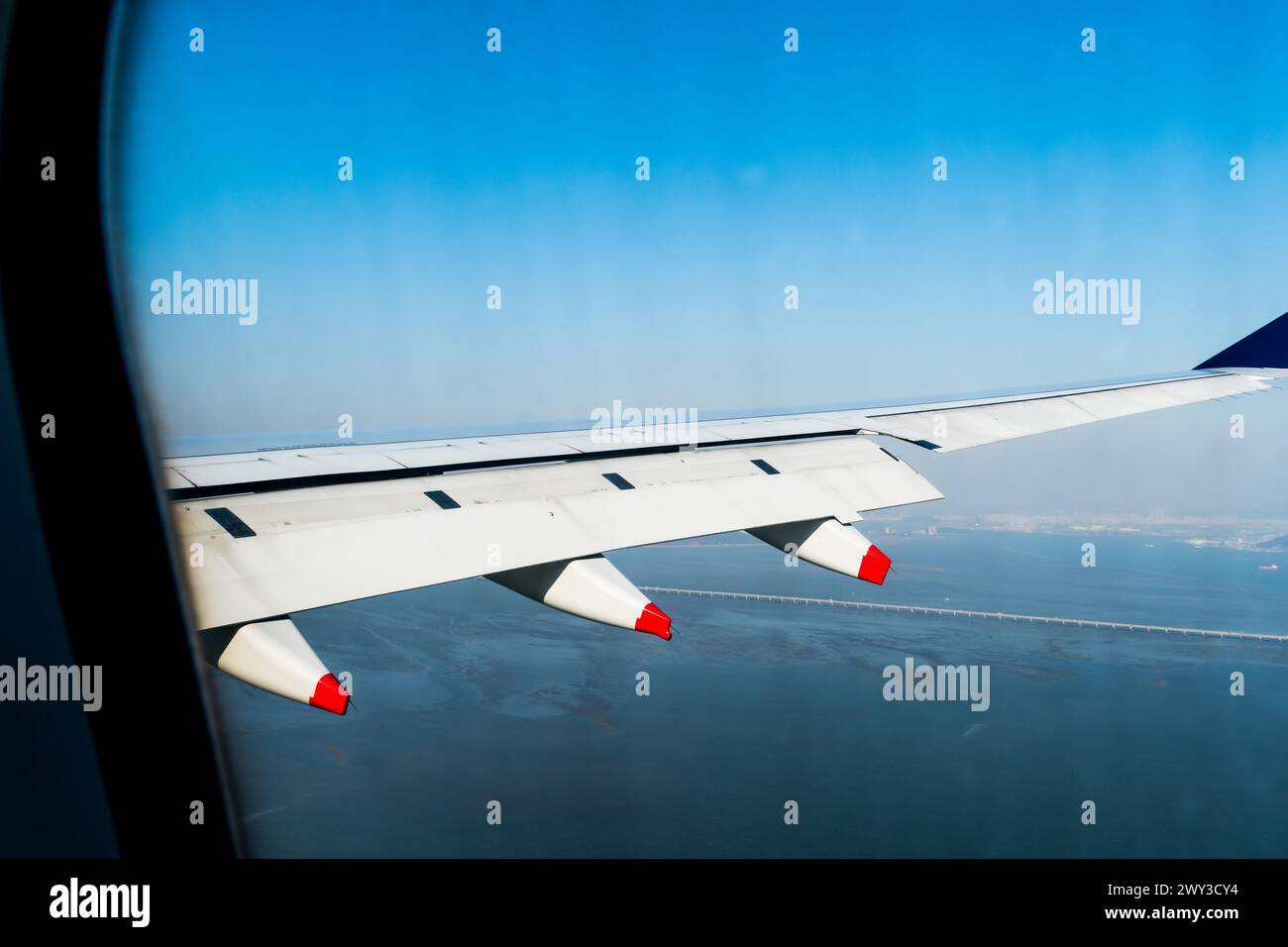 Aircraft wing with red tipped pillion in flight above ocean coastline ...
