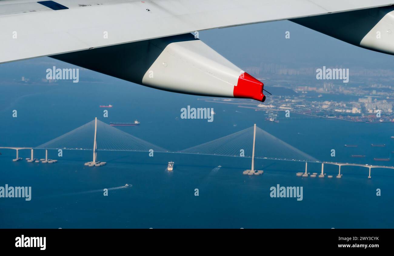 Aircraft wing with red tipped pillion in flight above water with city ...