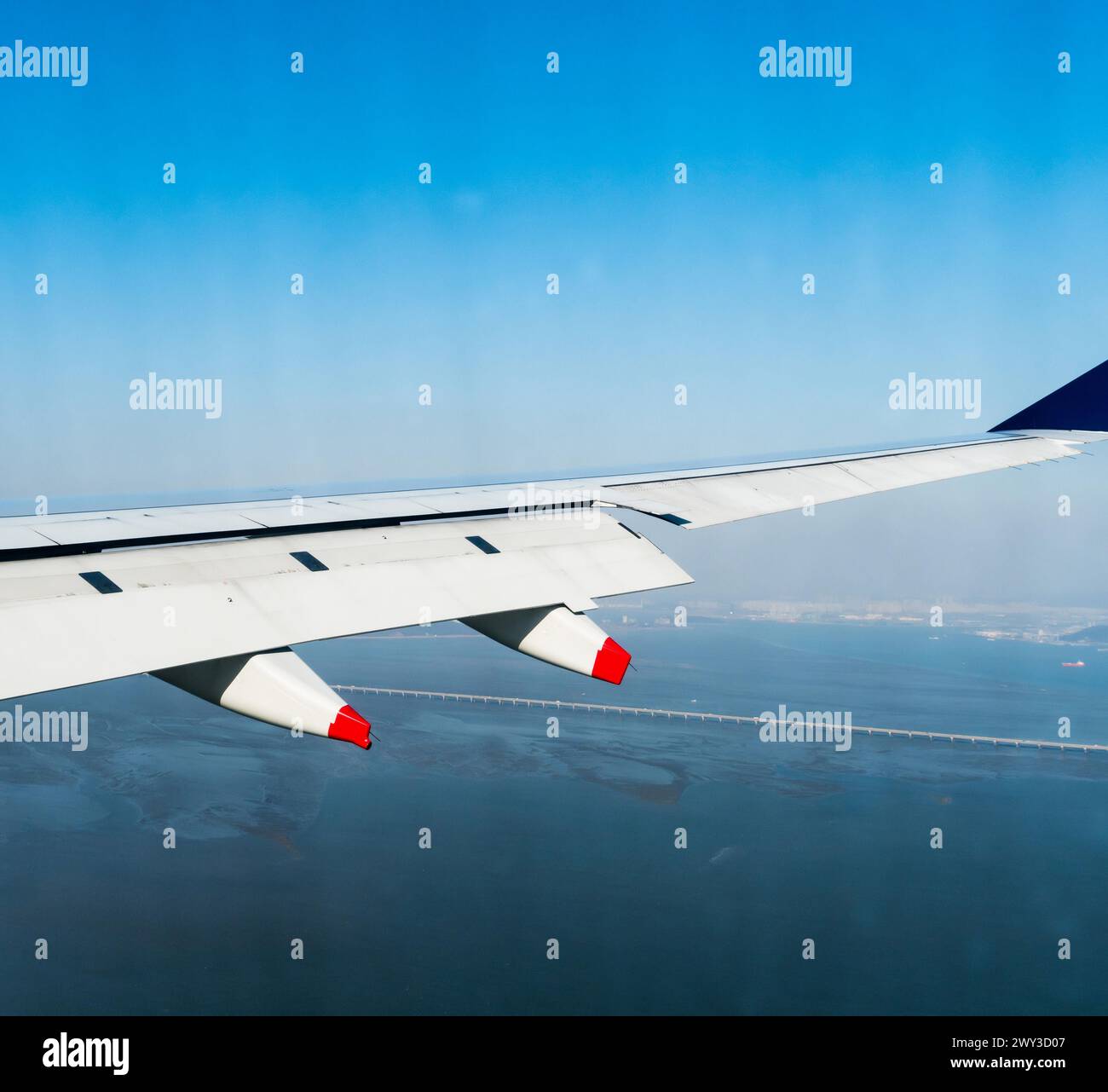 Aircraft wing with red tipped pillion in flight above ocean coastline ...