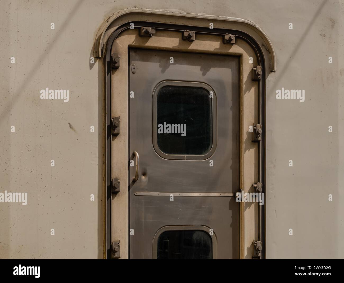 Close-up of a metallic train door with a small window and rivets, in ...
