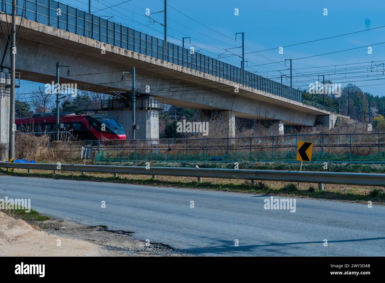 Engine of red passenger train traveling through concrete overpass in ...