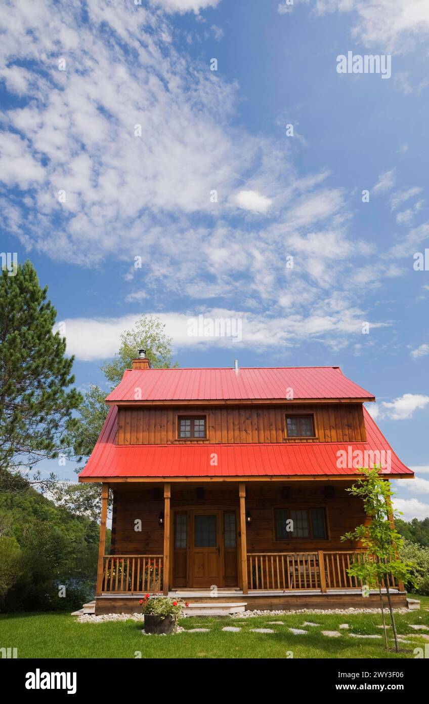 Small two story brown stained log cabin home with veranda and red sheet ...