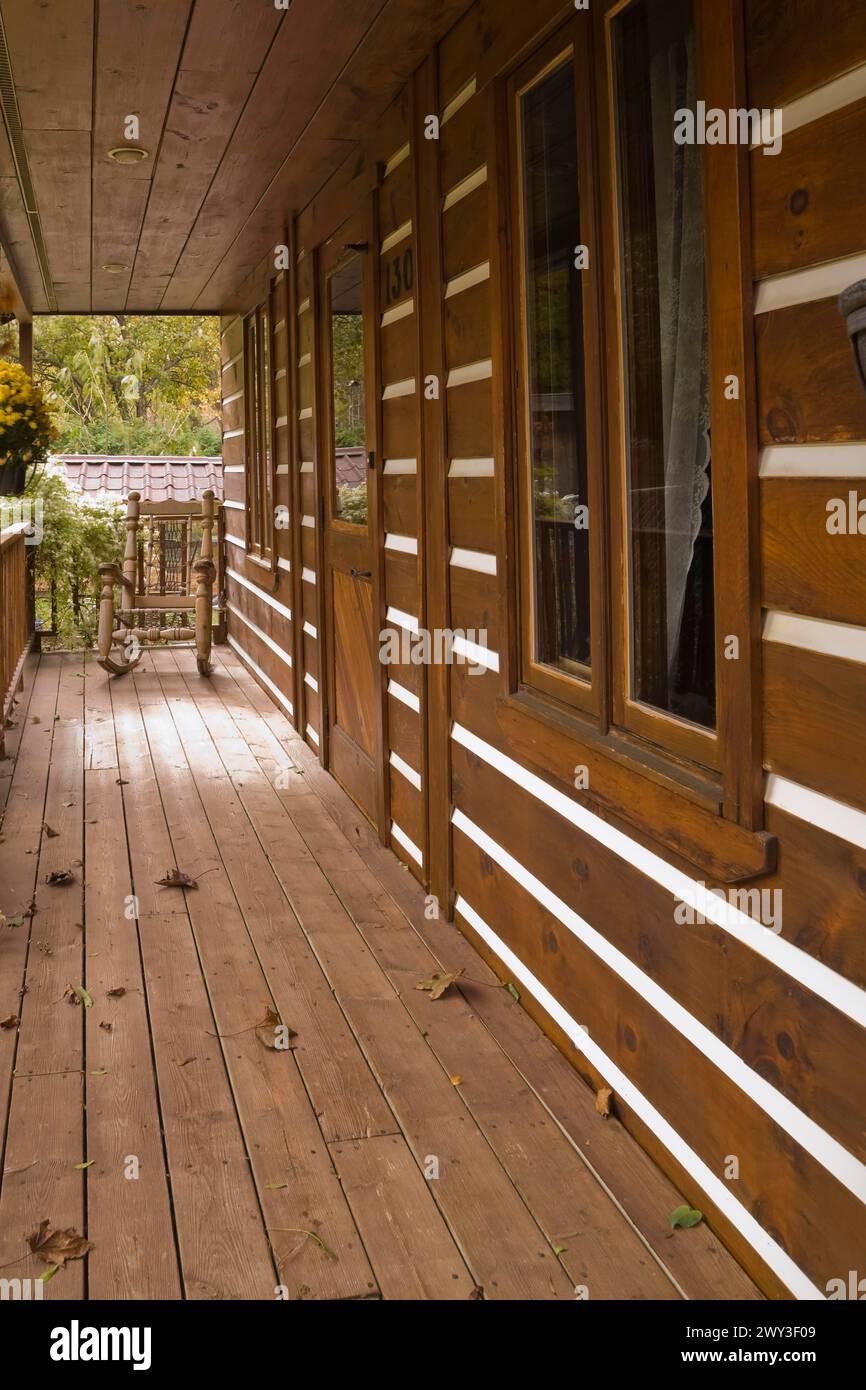Long old and worn brown stained veranda with pine wood rocking chair on ...