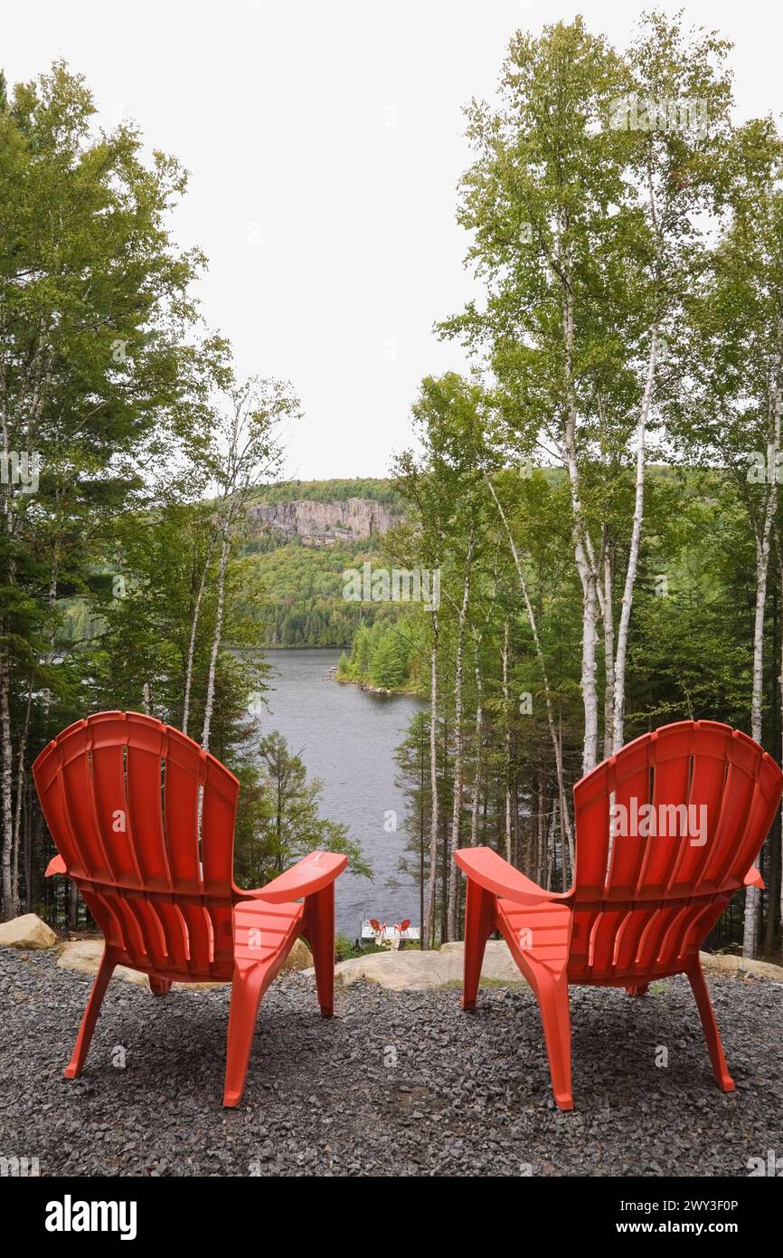 Two bright red plastic Adirondack chairs overlooking a calm lake ...