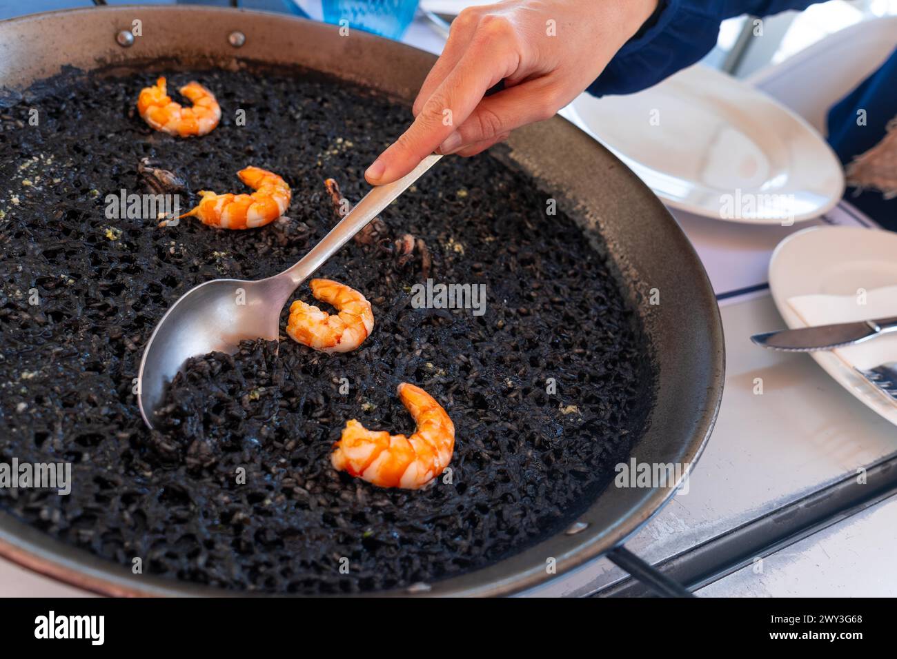 A spoon serving black rice with prawns and squid, a dry rice, cooked in ...