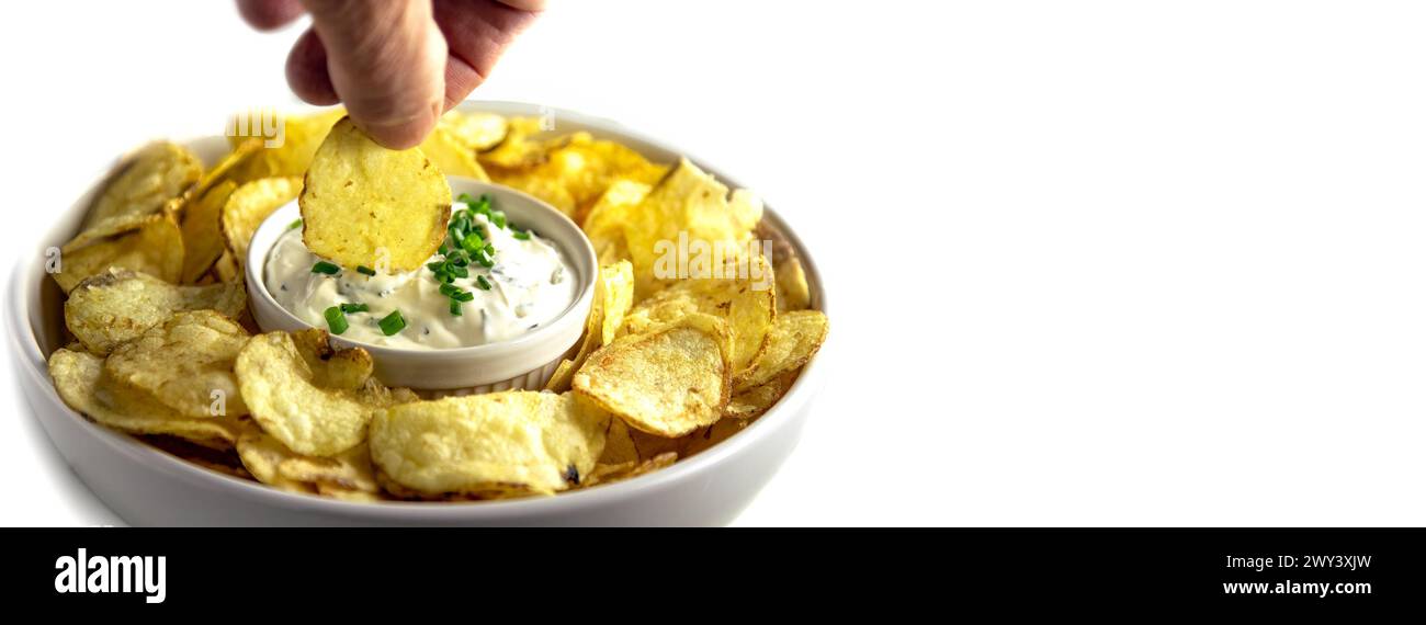 Panorama of man's hand holding potato crisp about to dip it into sour ...