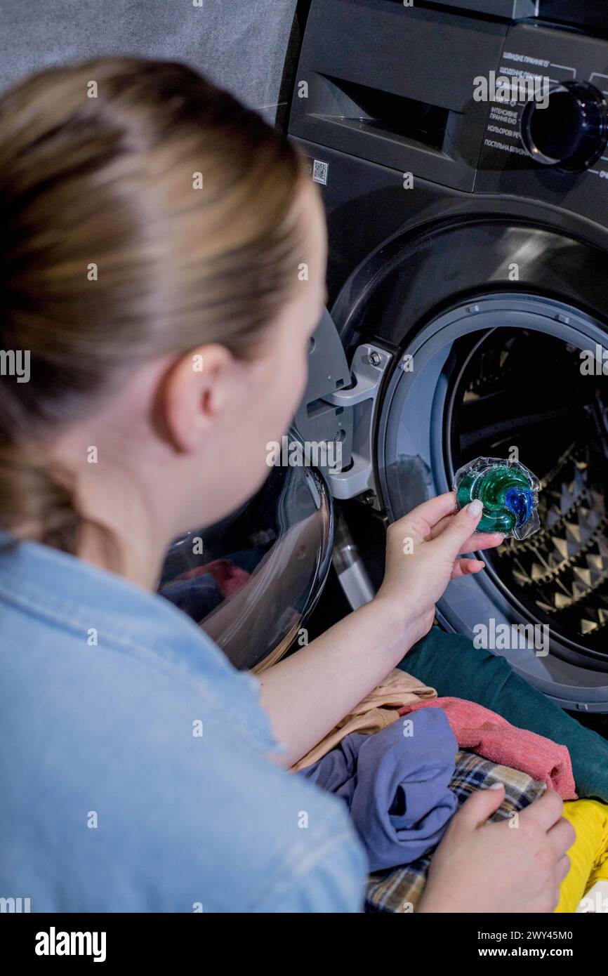 Woman putting laundry detergent capsule into washing machine indoors ...