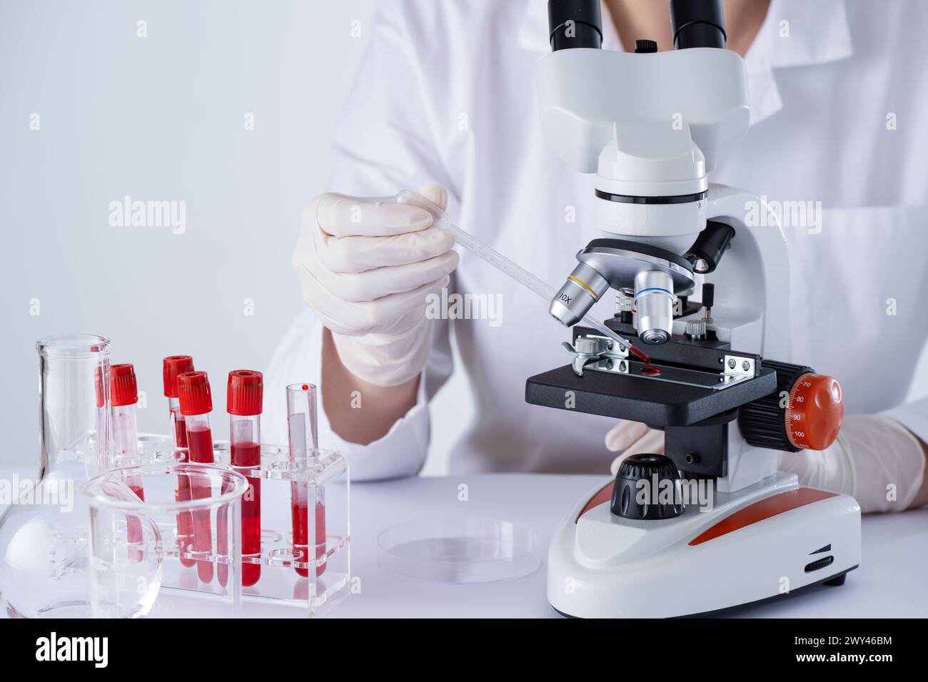 A scientist is using a microscope to examine a blood sample. Test tubes ...