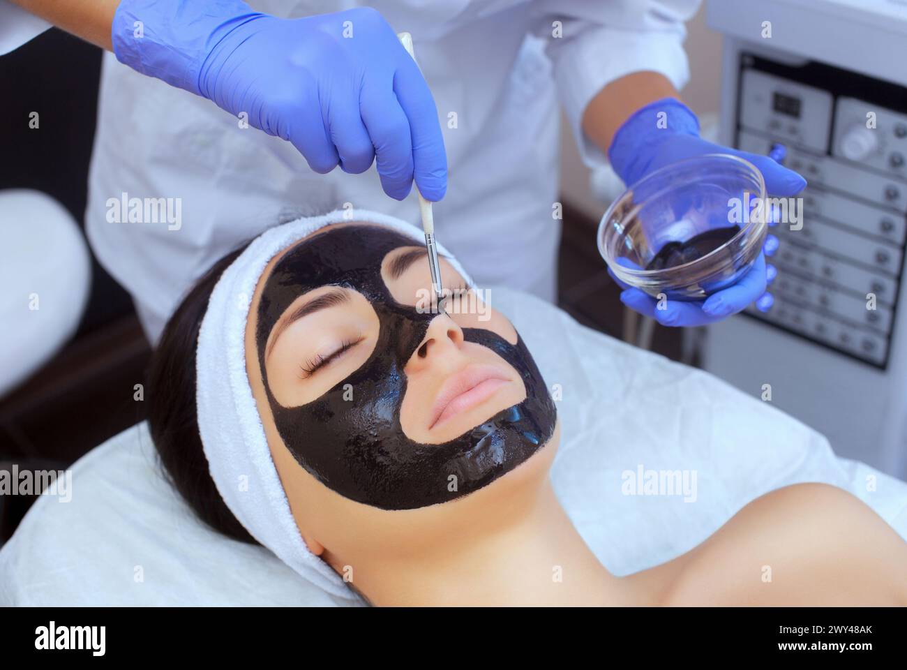 The procedure for applying a black mask to the face of a beautiful ...