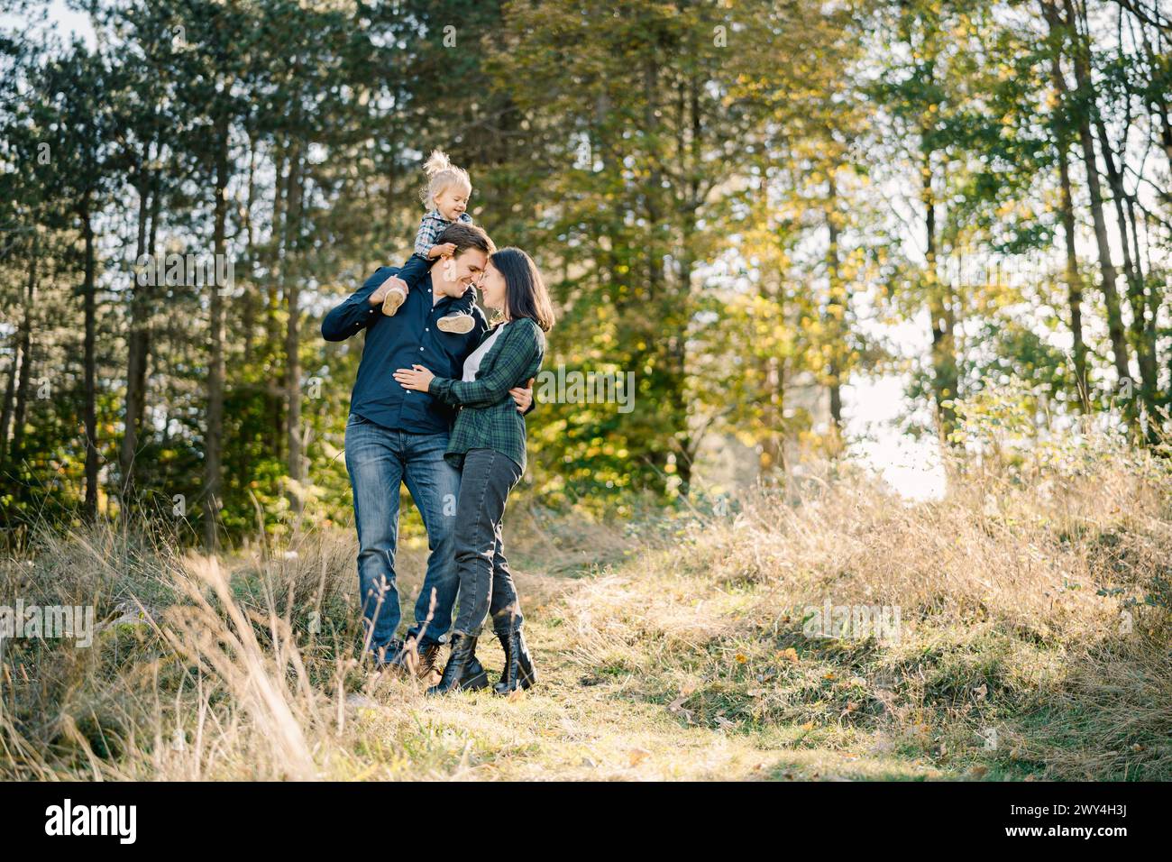Mom hugs dad with a little girl on his shoulders touching his forehead ...