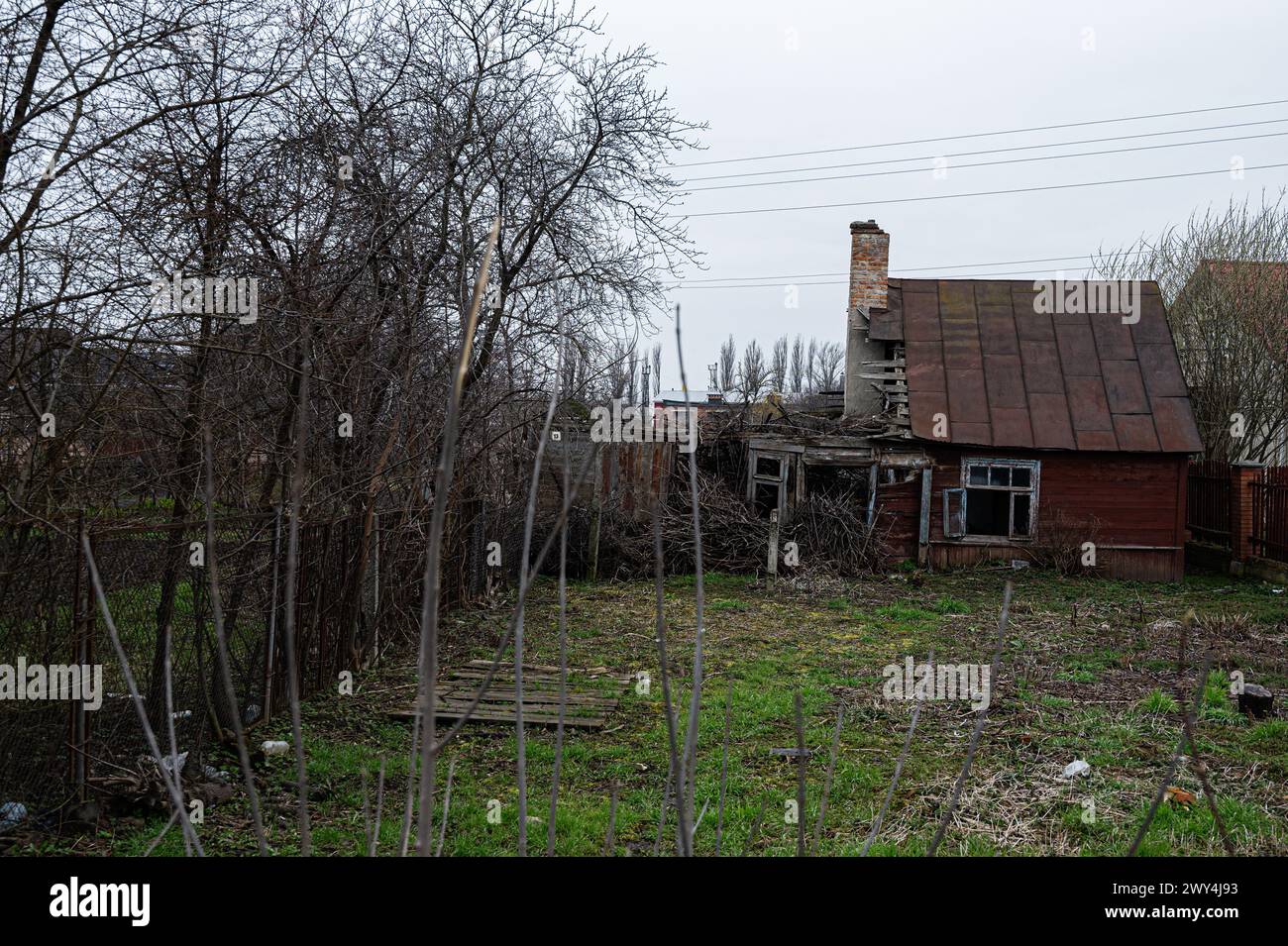 An old, decrepit wooden house with a rusty, broken roof and an overgrown garden, illustrating ...