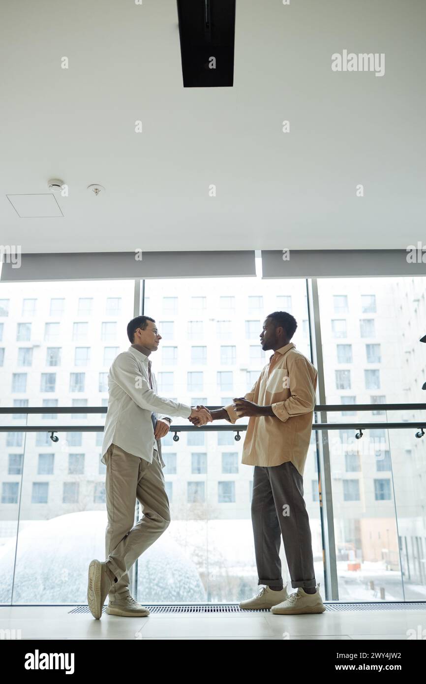 Vertical wide angle shot of two young male colleagues shaking hands ...