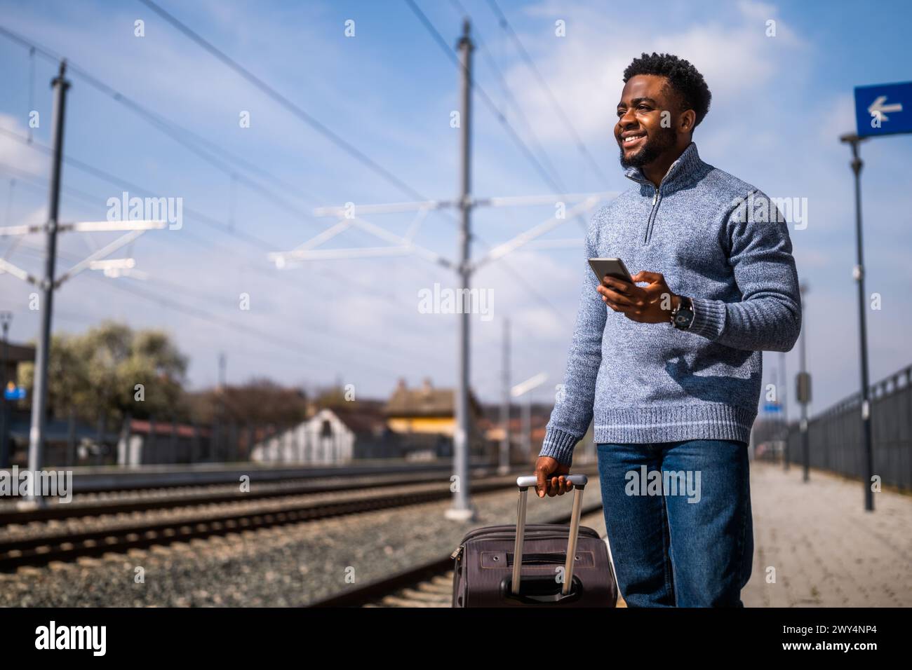 Happy man with a suitcase using phone while standing on the railway ...