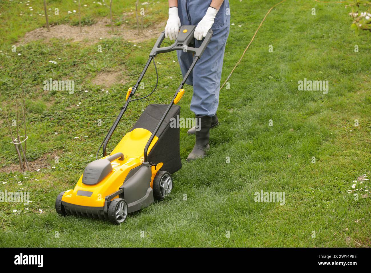 Gardener in black rubber boots trimming lawn with mower Stock Photo - Alamy