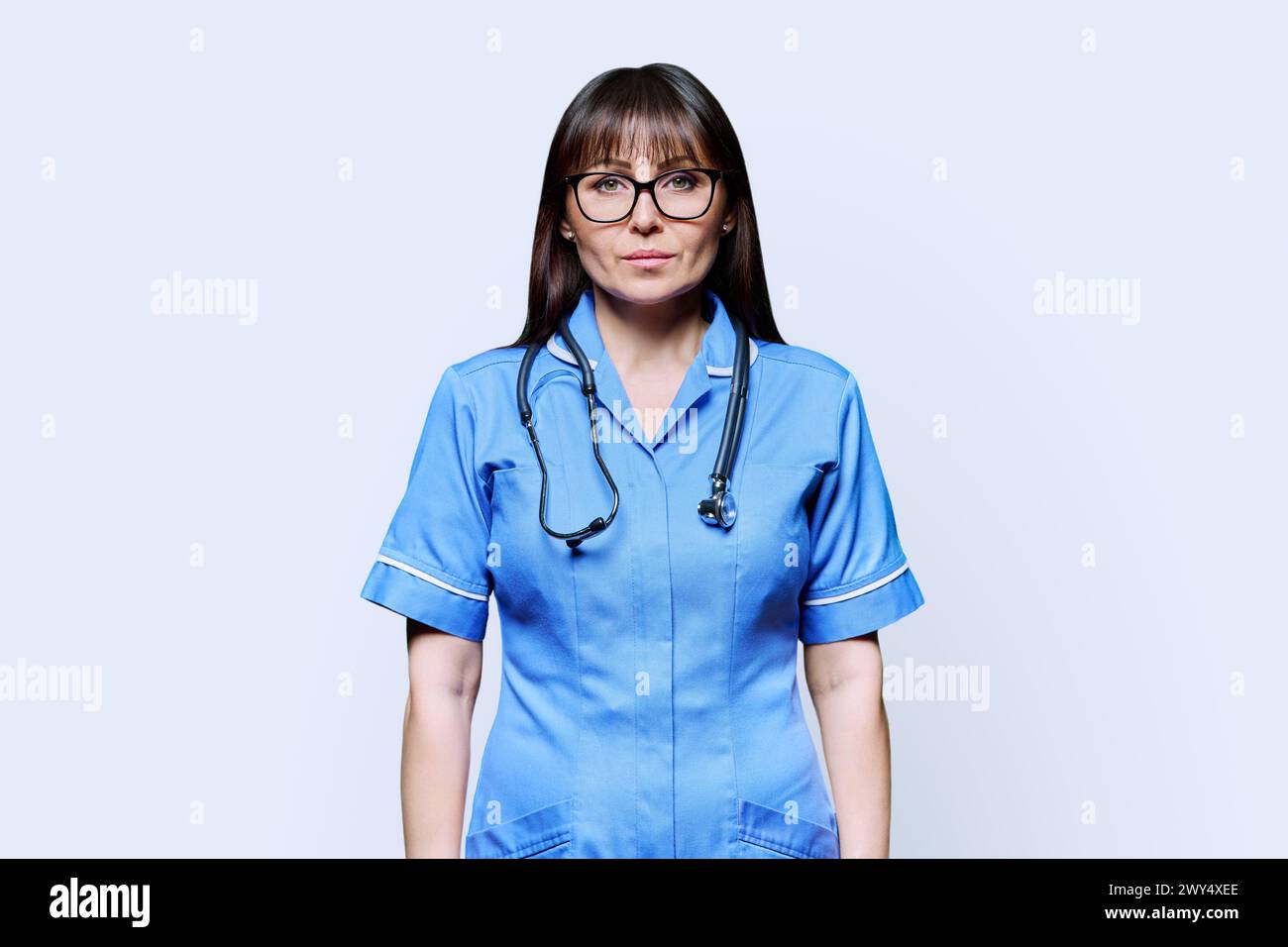 Portrait of serious female nurse in blue with stethoscope on white ...