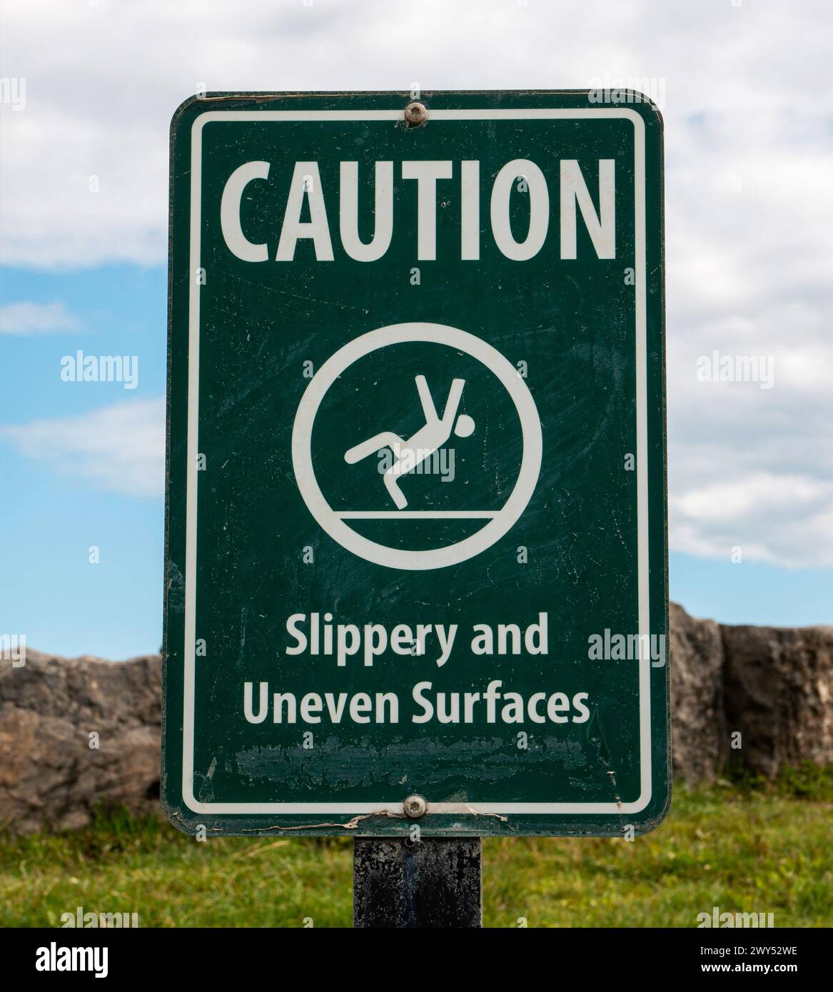 A green sign cautioning about slippery and uneven surfaces, warning ...