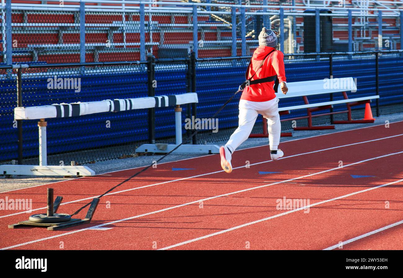 One male high school runner running while pulling a sled with weight on ...