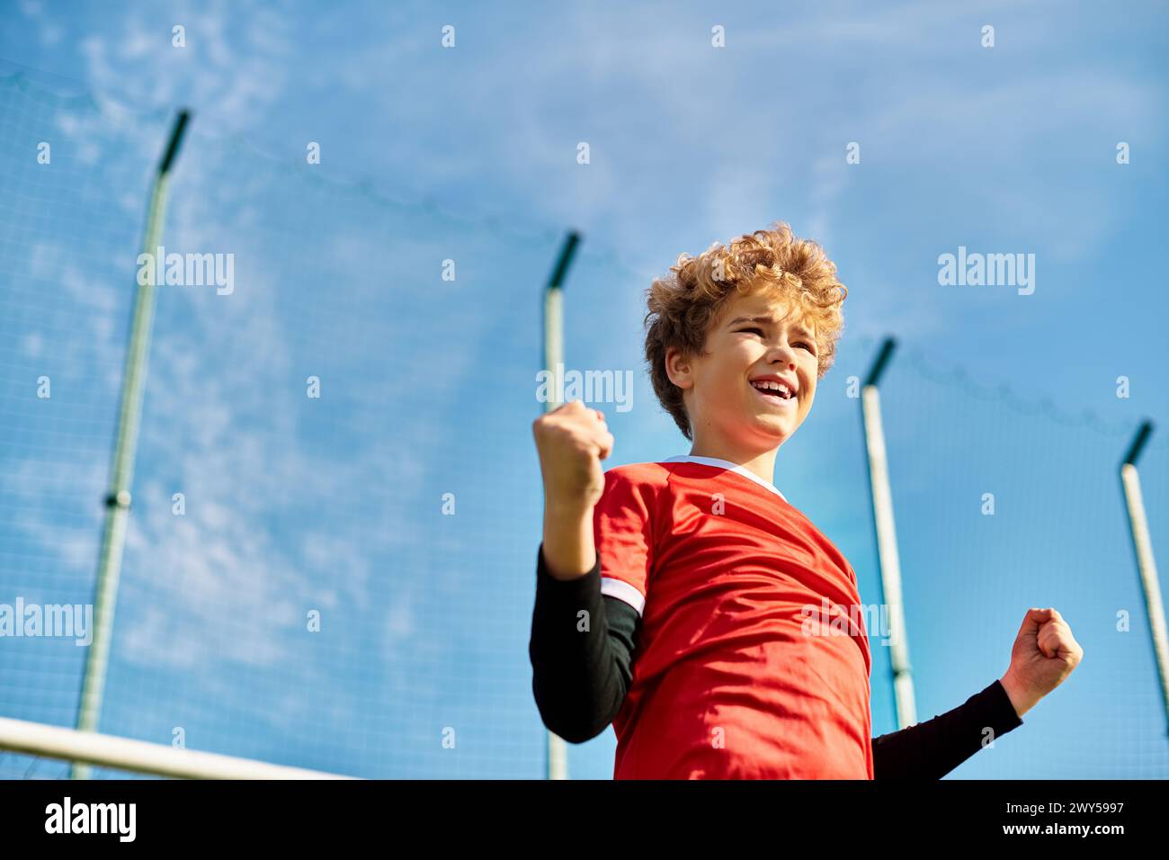 A young boy in a vibrant red shirt stands confidently holding a ...