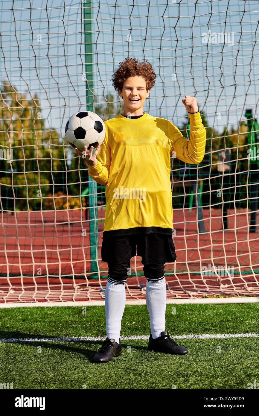 A young boy in a soccer uniform stands confidently, holding a soccer ...