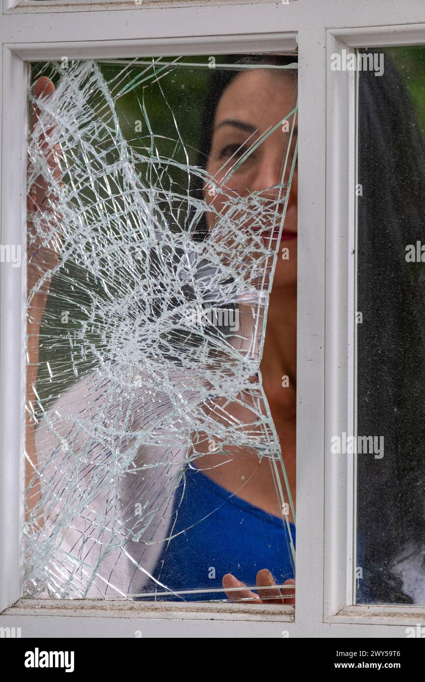 A woman peers through a shattered window, her gaze intersected by the ...