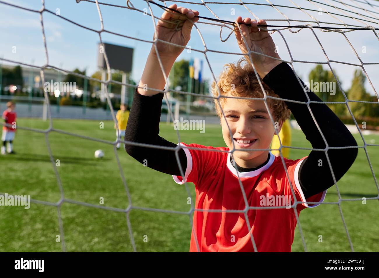 A young boy stands confidently in front of a soccer goal, focused on ...