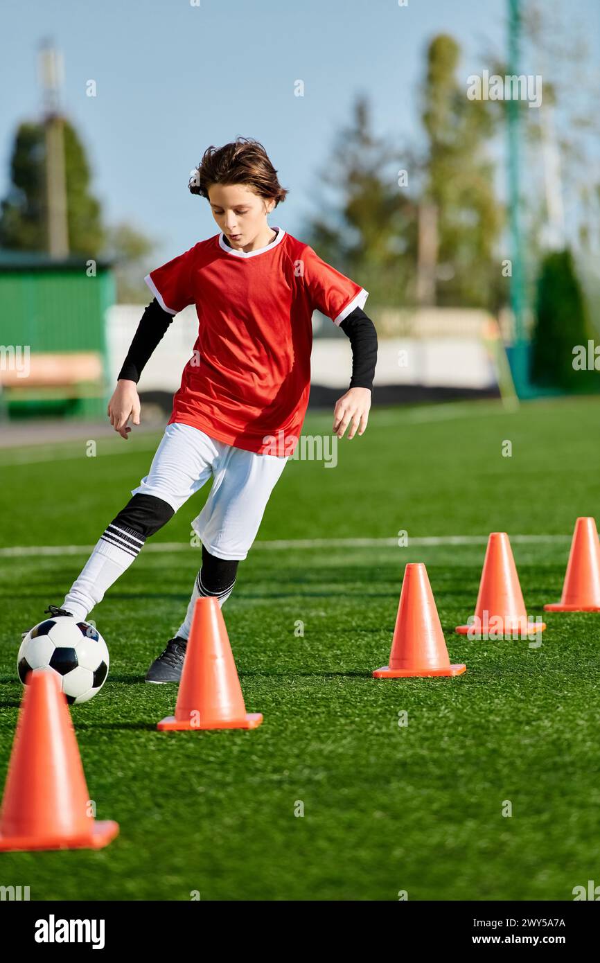 A young boy energetically kicks a soccer ball around orange cones ...