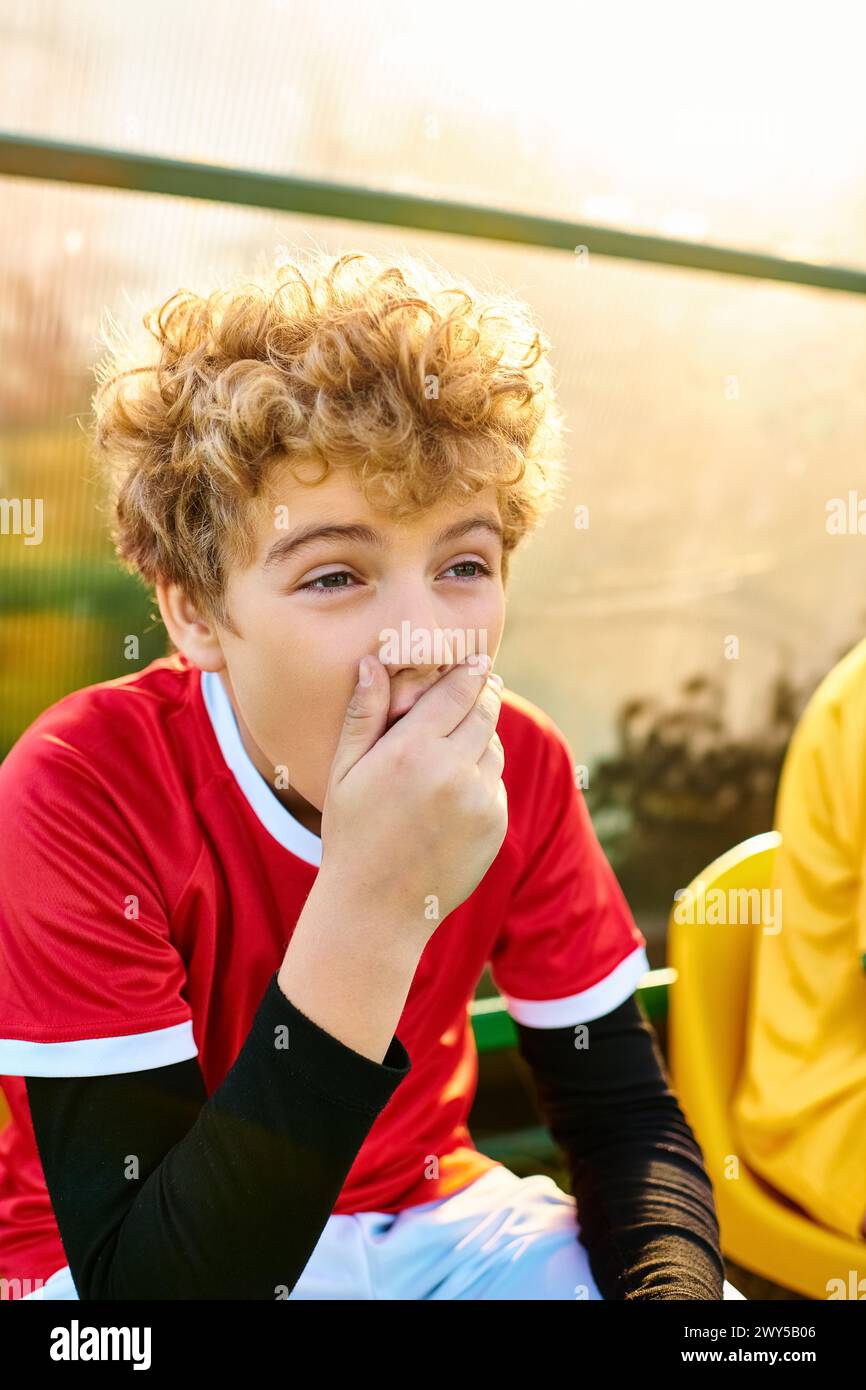 A young boy with a pensive expression sits on a bench, his hand gently ...