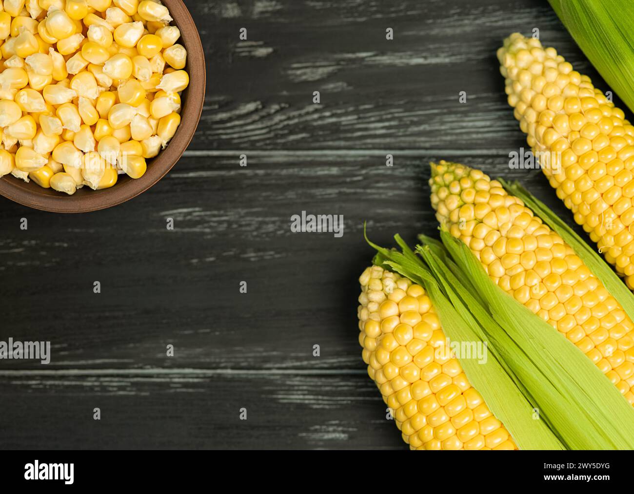 open cobs of sweet corn and corn kernels on a dark wooden background ...