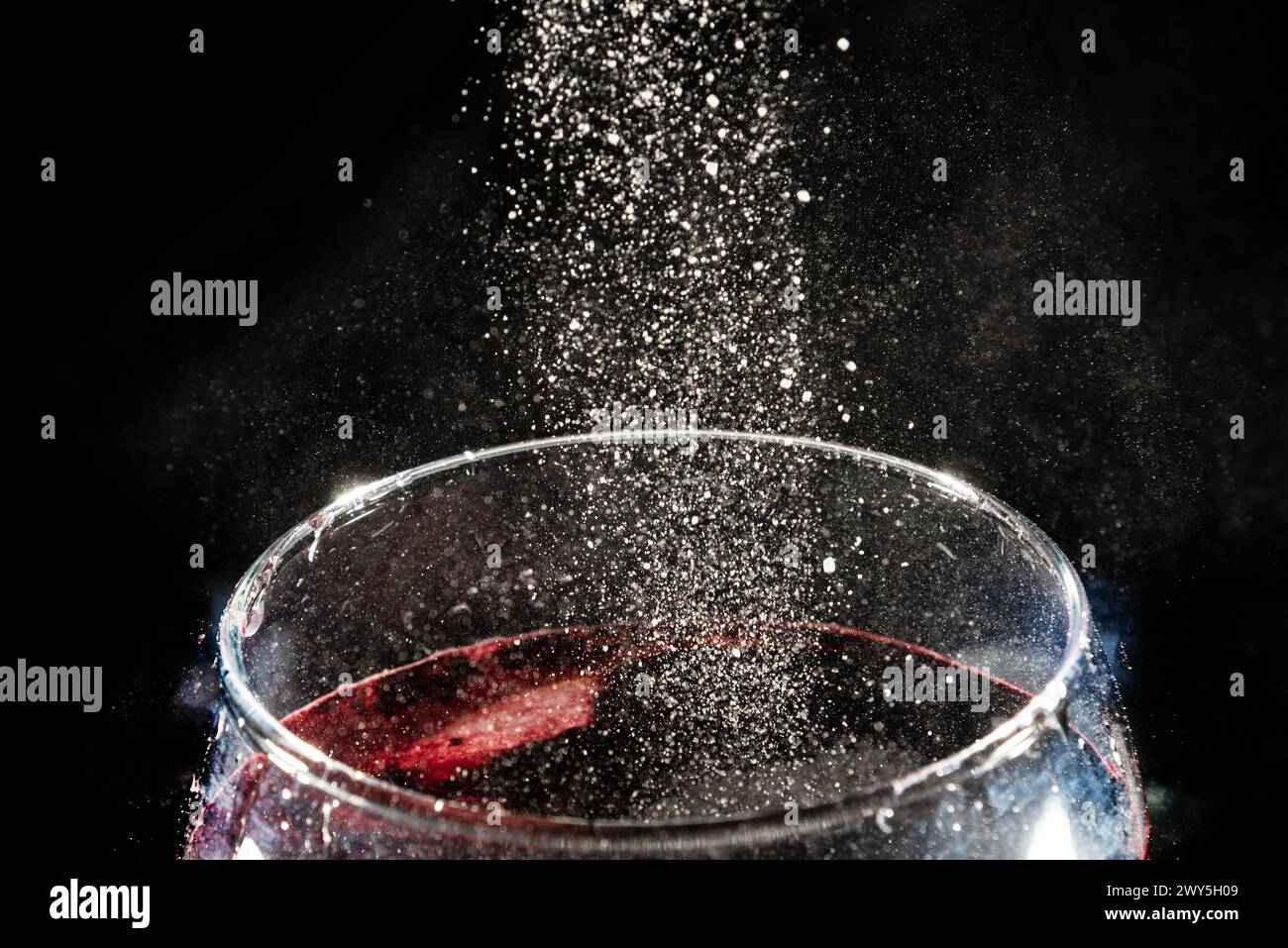 White powder falling into a transparent glass cup filled with wine ...