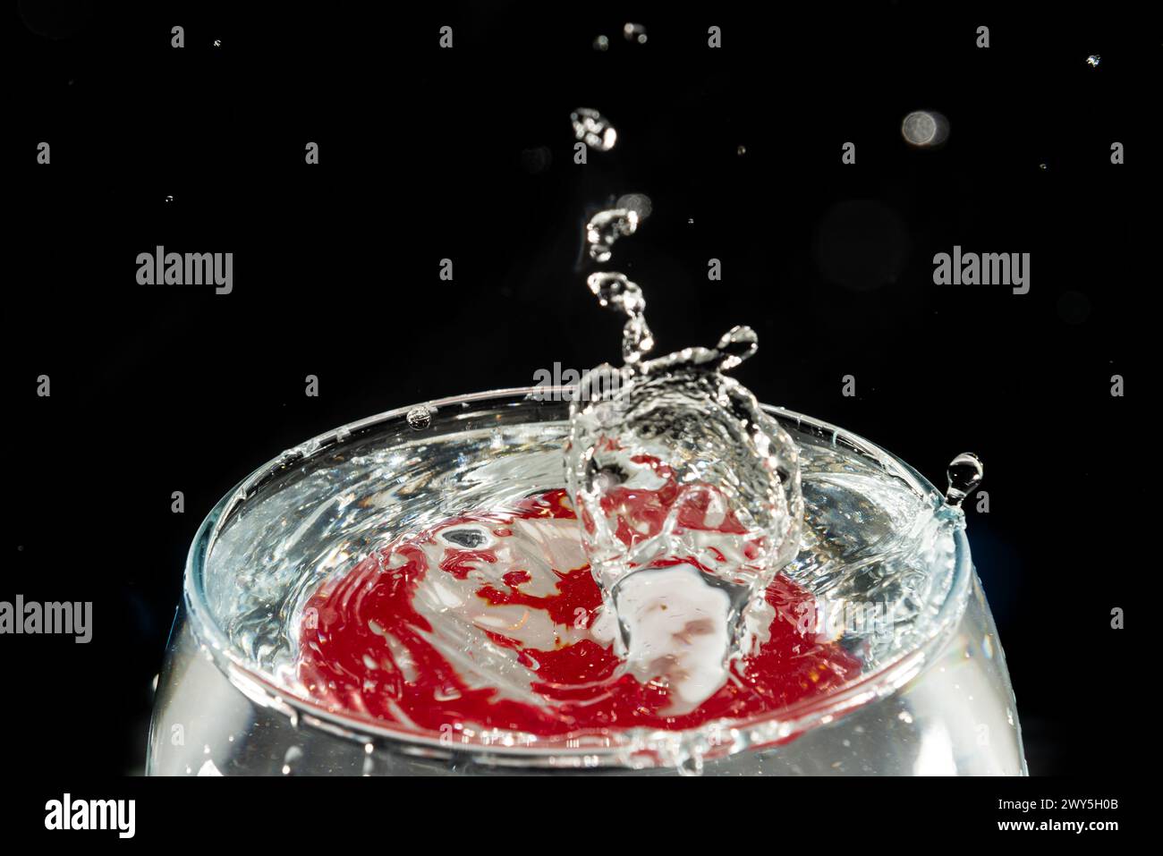Transparent glass bowl, filled with water, with red reflection and ...