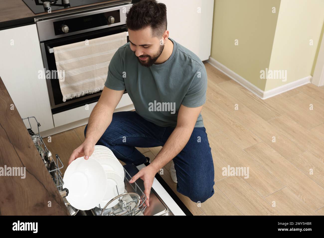 Smiling man loading dishwasher with plates in kitchen. Space for text ...